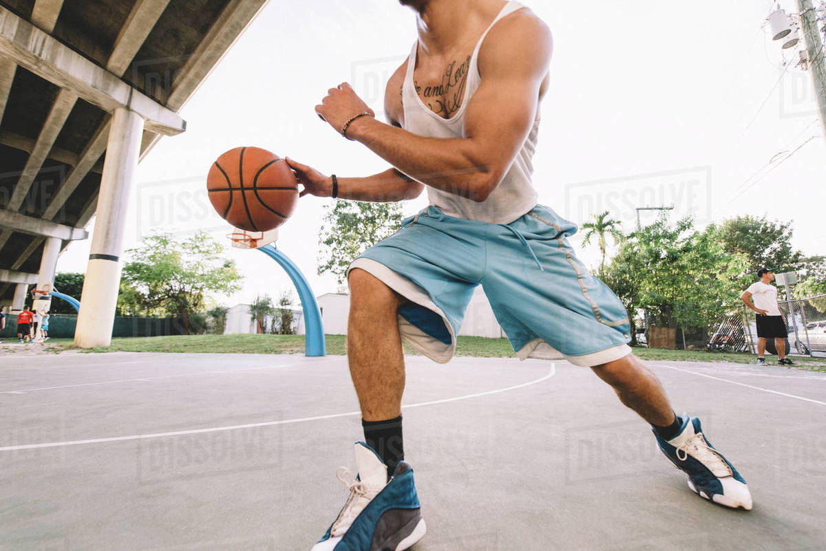 Cropped view of man on basketball court running, bouncing basketball ...