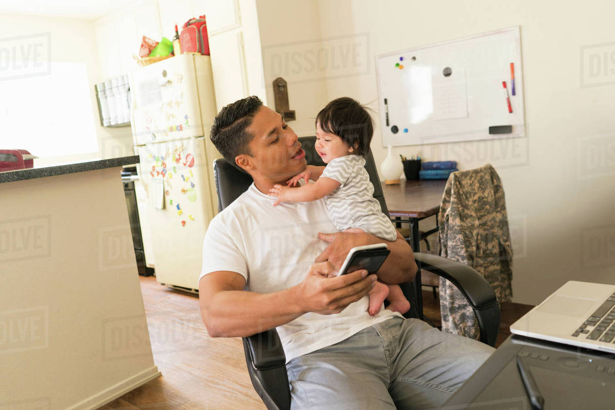 Father using mobile phone and carrying baby in arms - Stock Photo ...