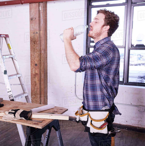 Carpenter in workshop drinking from water bottle - Stock Photo - Dissolve