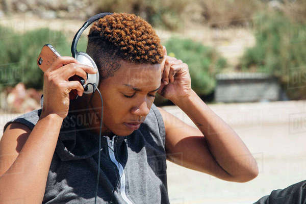 Woman wearing headphones holding smartphone looking down - Royalty-free ...