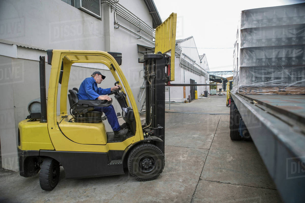 Forklift driver loading pallet onto truck at packaging factory - Stock ...