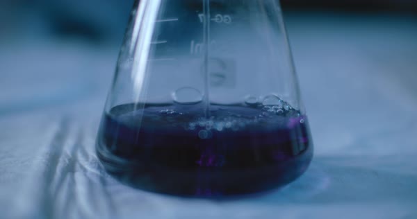 Scientist adding a purple liquid to a conical flask to test chemicals ...
