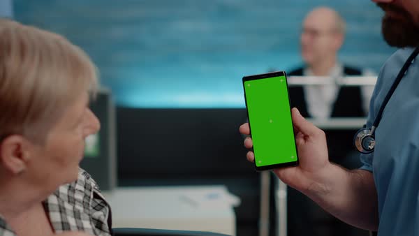 Close up of nurse vertically showing phone with green screen to senior ...