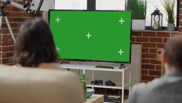 Young people on sofa looking at television with green screen display ...