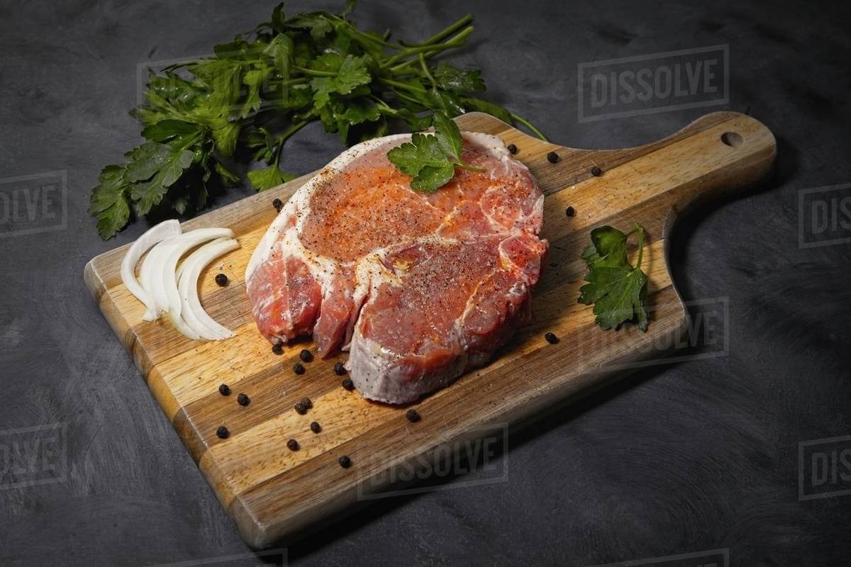 An overview of a raw pork chop cutlet on a wooden cutting board with ...