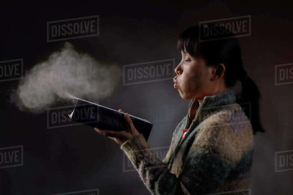 Asian woman blows dust off an old dictionary in this concept image ...