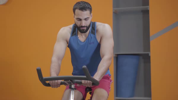 Portrait of concentrated muscular Middle Eastern man riding exercise ...
