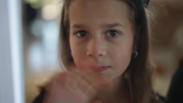 Close-up face of a little girl knocking in glass door looking at camera ...