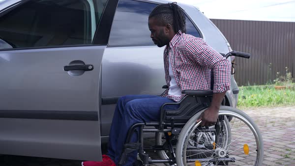 Man riding wheelchair to car making effort sitting on driver's seat ...