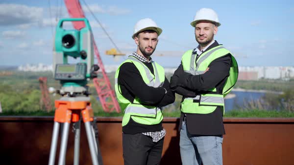 Portrait of two confident young engineers with crossed hands looking at ...