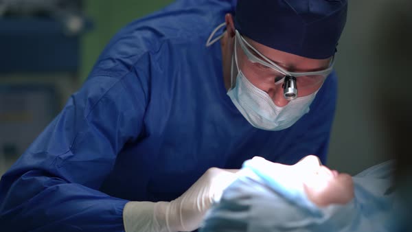 Concentrated surgeon making dissection on face of patient lying on ...