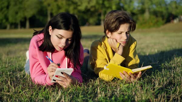 Teenage boy and girl reading writing lying on sunny meadow in park ...