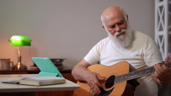 Curios old Caucasian man sitting with guitar playing watching online ...