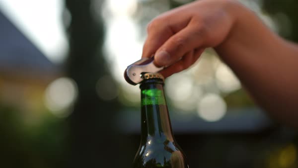 Close-up. A man's hand opens a green glass bottle using a beer opener ...