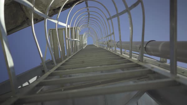 Bottom view of large ladder on cement storage silo with clear blue ...