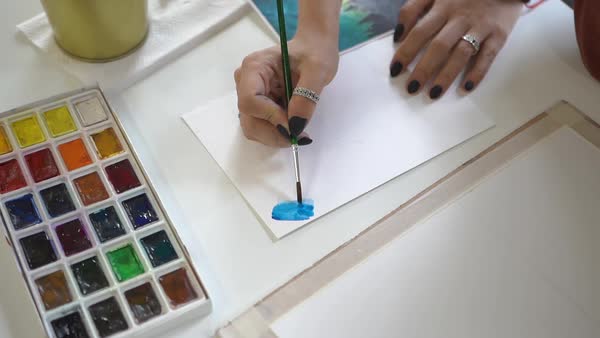 The girl draws on white paper with a brush and blue paint a drawing on ...
