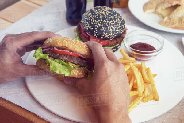 Man eating burgers at table, pov view - Royalty-free Stock Photo | Dissolve