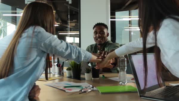 Office workers doing team building exercise stacking hands together in ...