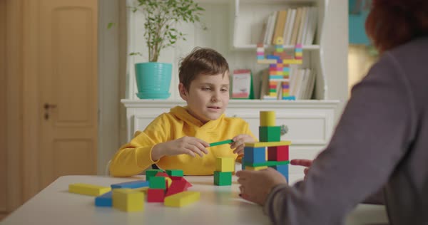 Autistic boy building with color wooden blocks. Teacher gives ...