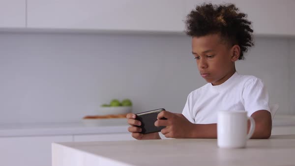 African american teenager boy playing games on phone. Addicted child ...