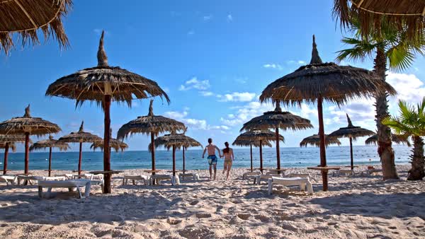 Couple on sand beach running towards sea. Low angle view of straw ...