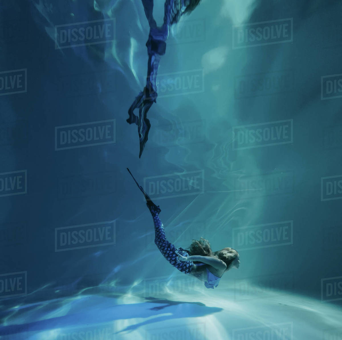 Beautiful young woman with mermaid tail swims and dives under sunlit ...