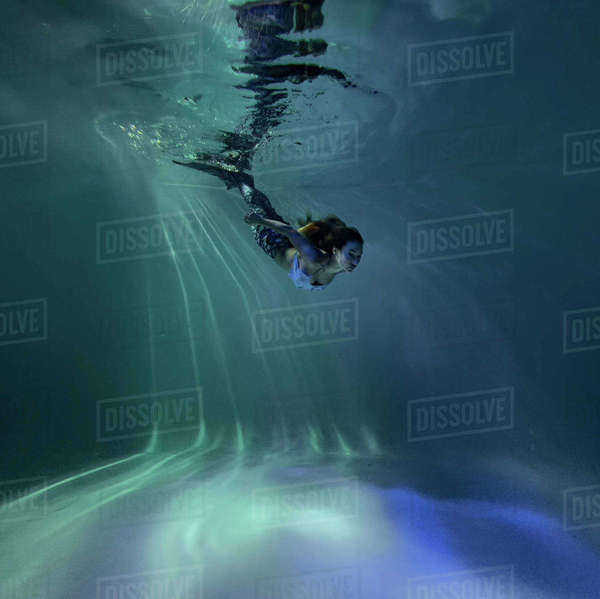 Beautiful young woman with mermaid tail swims and dives under sunlit ...