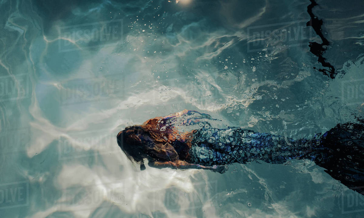 Beautiful young woman with mermaid tail swims and dives under sunlit ...