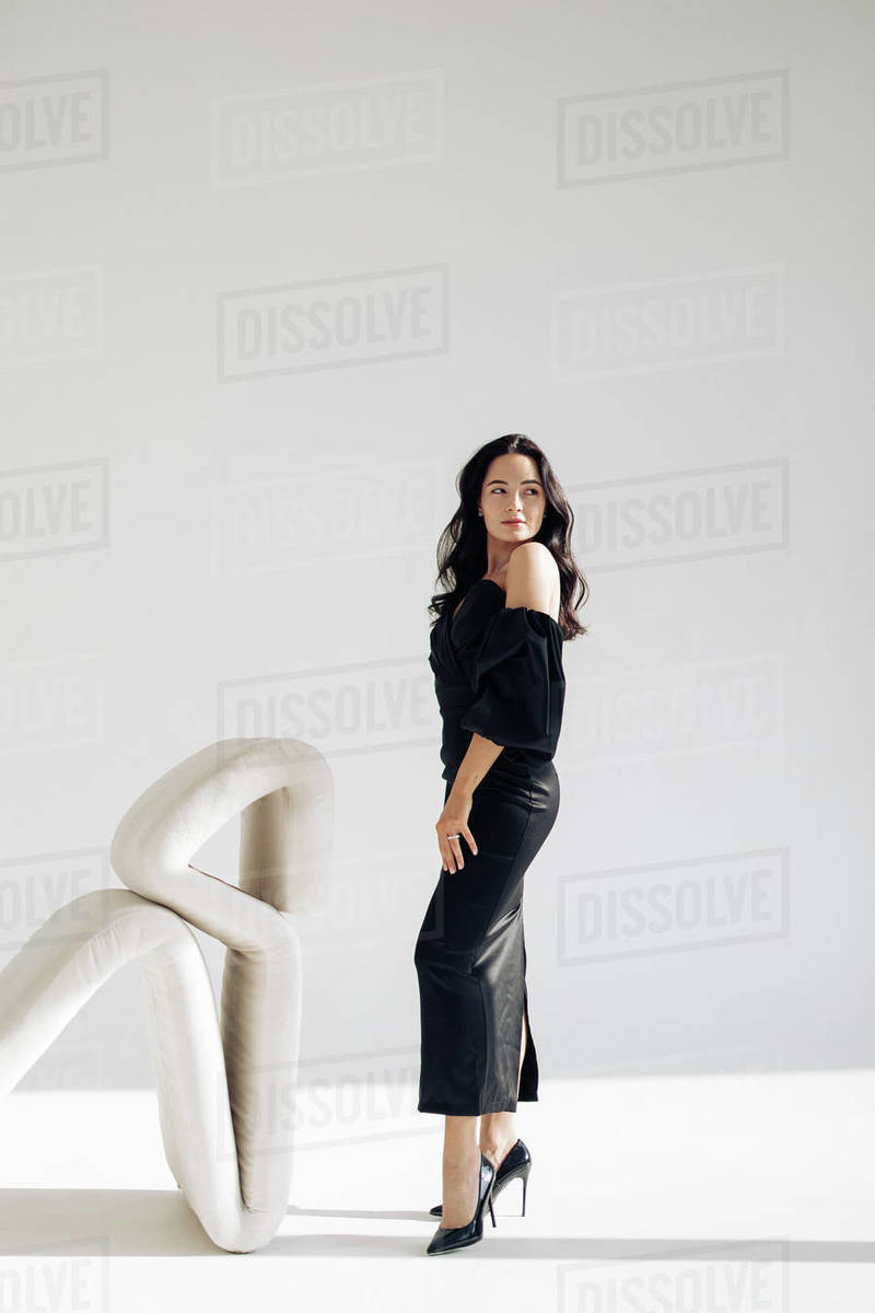 Young woman poses in studio near armchair in long black dress and high ...