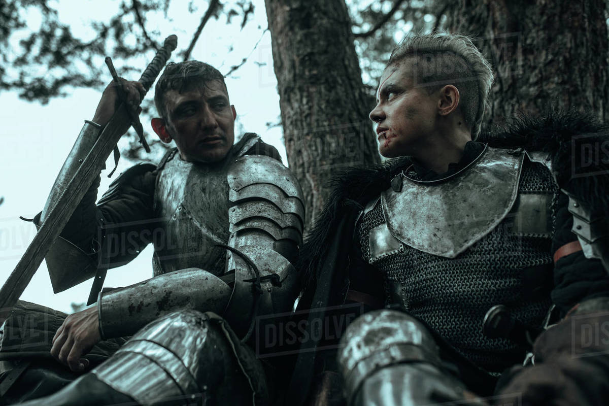 Two tired medieval warriors knights in chain mail armour sit and rest ...