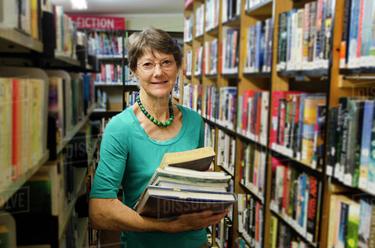 A woman librarian holds books beside bookshelf in library. - Royalty ...