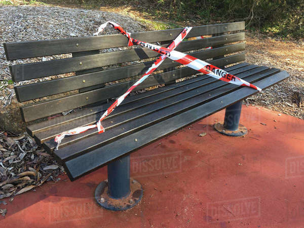 An empty park bench with caution danger warning tape under new ...
