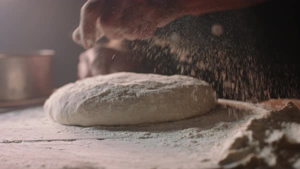 Closeup shot of hands of senior bakery chef applying flour on dough ...