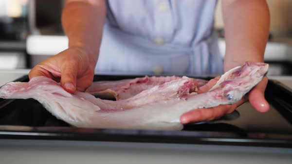 Hands prepare sea bass fish for baking on a baking sheet. Cooking ...