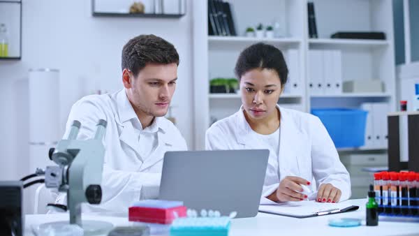 Male and female researchers checking test results on laptop, writing ...