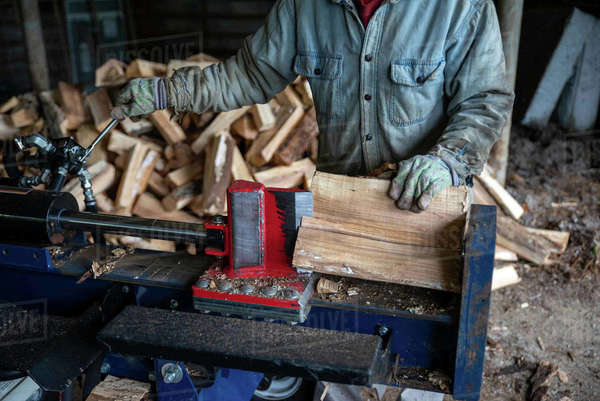 Work man splits wood with a hydraulic log splitter. Blade is seen ...
