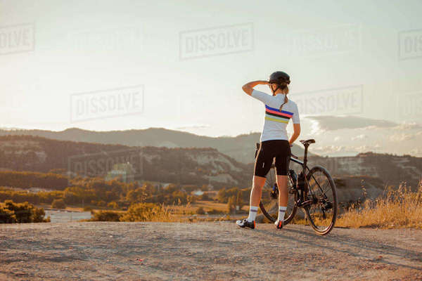 Fit young female cyclist, standing with her bike in hand, admiring the ...