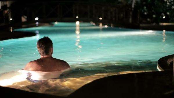 Man sitting in luxury hotel swimming pool at night - Stock Video ...