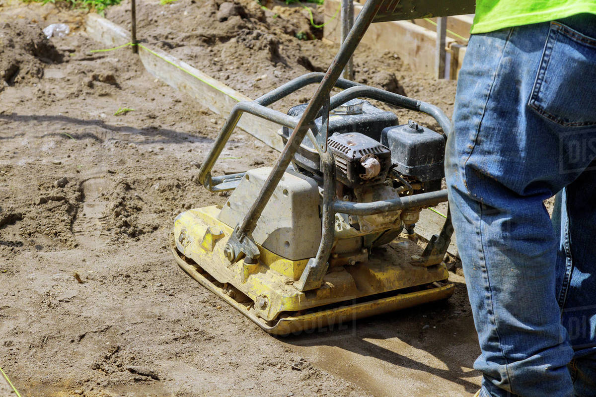 Worker uses compactor to vibratory hammer power tool at soil at ...