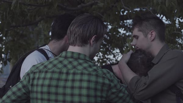 Hand-held shot of a young man crying and being comforted by his friends ...