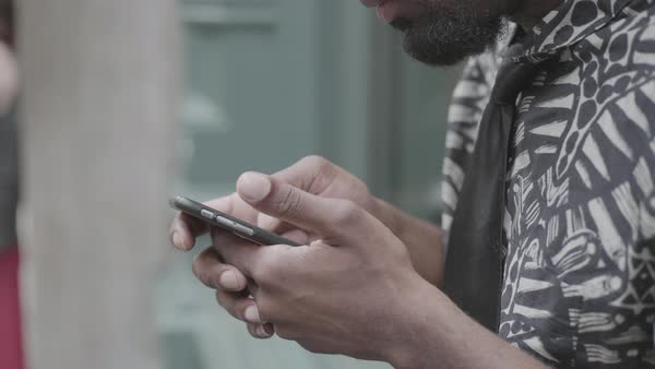 Close-up shot of a young man using a smartphone while standing outdoors ...