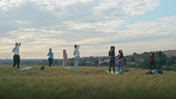 A group of women doing yoga outdoors. breathing exercises in nature in ...