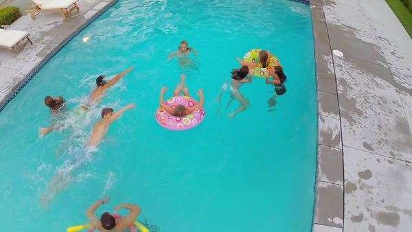 Teen friends have a fun chicken fight at a pool party, girls cheer them ...