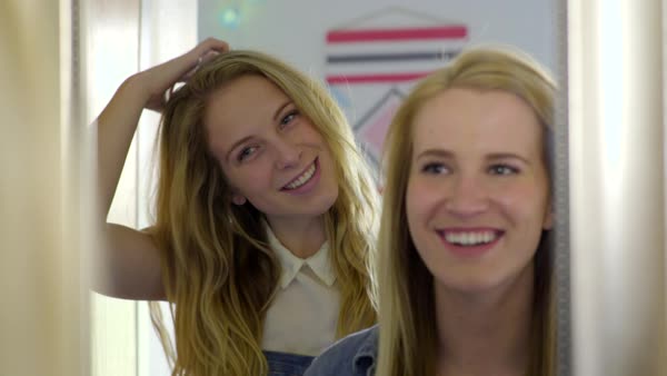 Two girls primp in a mirror together, one makes a funny face and they ...