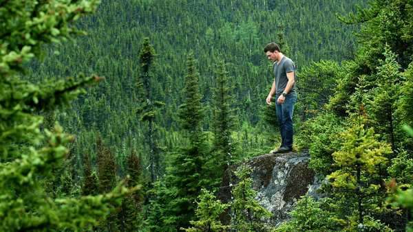Man walking to the edge of a forest cliff and looking to the horizon ...
