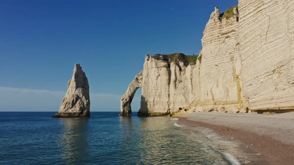 A sharp triangular rock peak sticking out of the water next to a ...