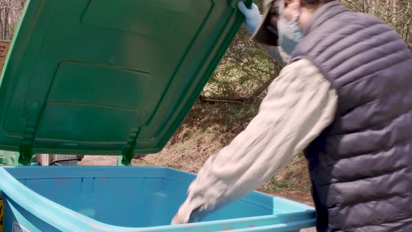 Man wearing a mask and gloves throwing away a bag of garbage in an ...