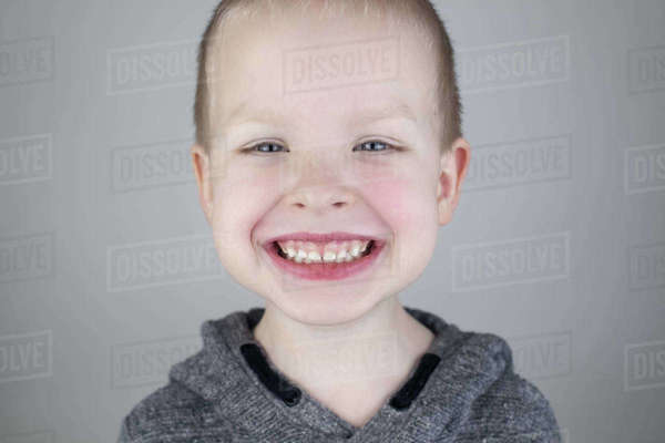 Close-up of a blond boy who smiles into the frame. White milk teeth ...