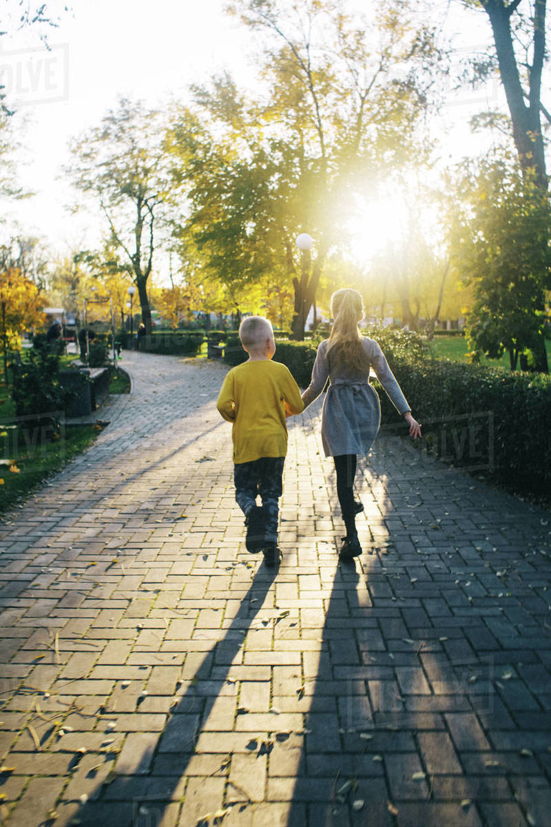 Brother and sister in park. Boy and girl hold hands and run along the ...