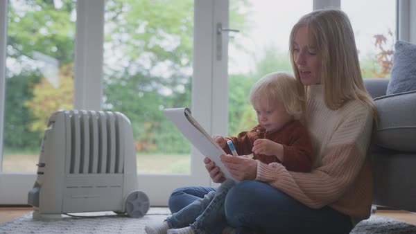 Mother and son sitting on floor next to portable plug in radiator ...